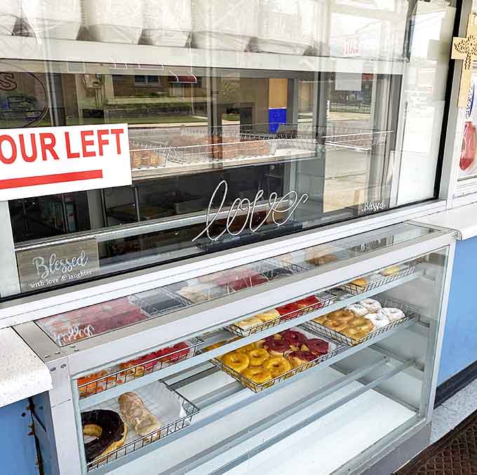 Peek through the display window where trays of freshly made donuts await, their glazed surfaces glistening with promise of sweetness to come.
