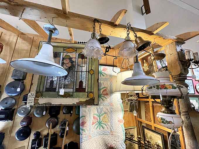 Vintage lighting fixtures dangle from wooden beams like strange fruit, each one carrying the energy of rooms they once illuminated.