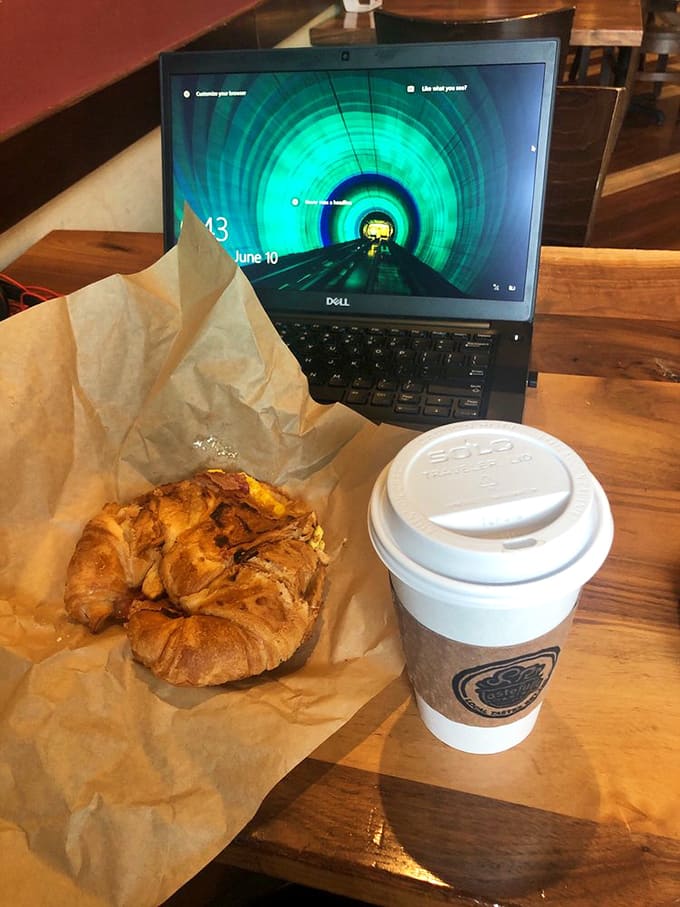 Morning multitasking at its finest: a buttery breakfast sandwich alongside a steaming cup of coffee &ndash; fuel for productivity or simply pleasure.
