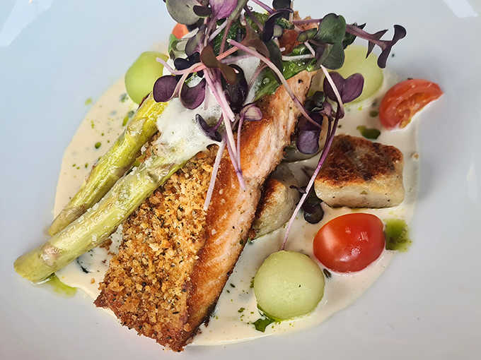 Perfectly seared salmon rests on a bed of creamy sauce, accompanied by asparagus and colorful microgreens &ndash; edible art that tastes even better.