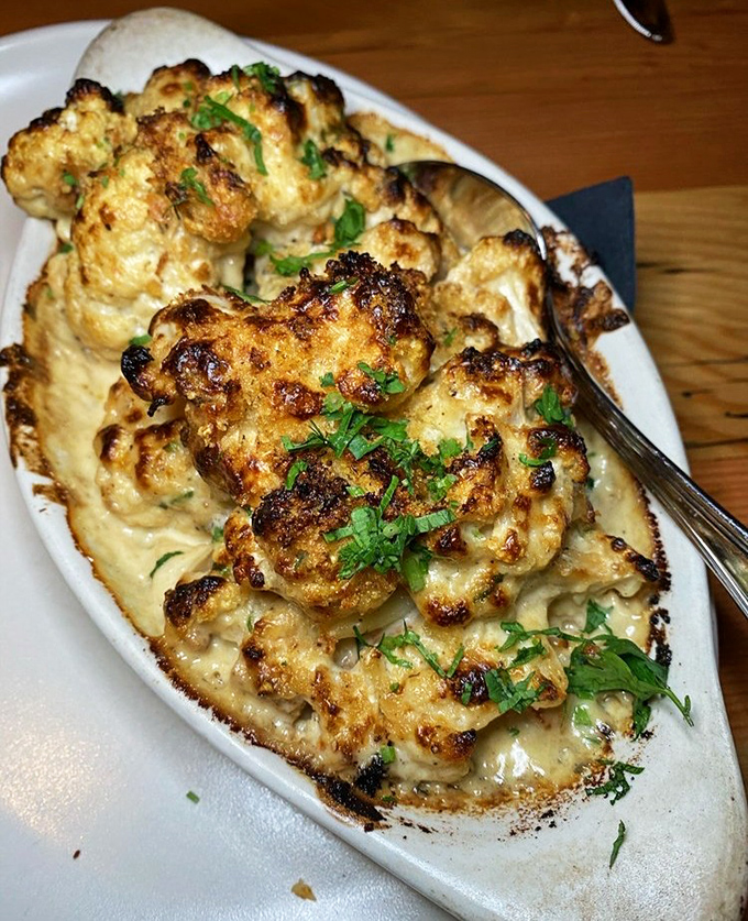 The legendary Cauliflower Gratinata arrives bubbling hot, its golden crown of cheese and herbs transforming a humble vegetable into the star attraction.