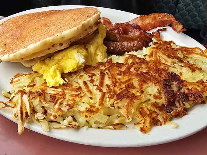 Golden hash browns, fluffy pancakes, and crispy bacon form the holy trinity of breakfast perfection on one glorious plate.