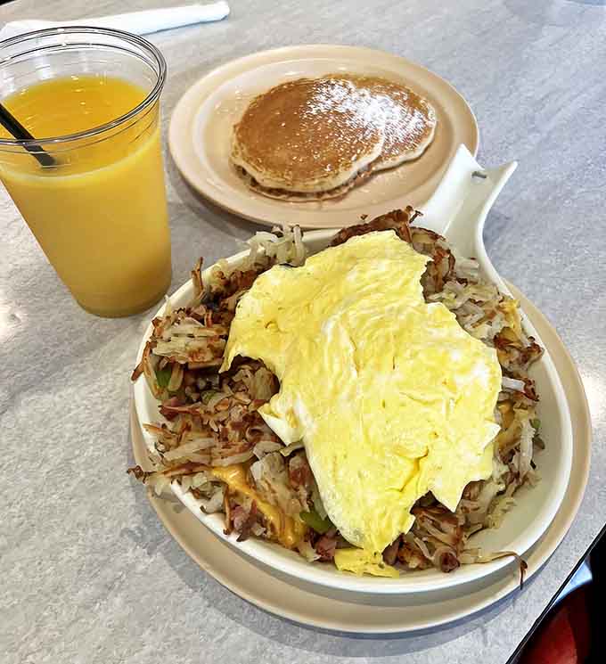 A perfect breakfast trifecta: golden hash browns, fluffy pancakes, and fresh orange juice – simple perfection on a plate.