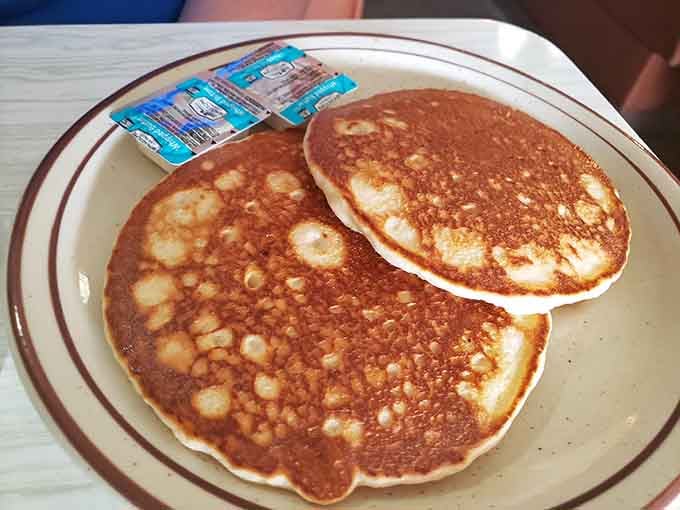 Two golden pancakes that could make a morning person out of anyone, each one a fluffy masterpiece ready to soak up butter and syrup in equal measure.
