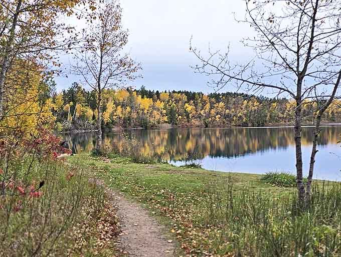 Autumn's golden touch transforms this lakeside path into a magical journey between fiery foliage and impossibly blue waters.