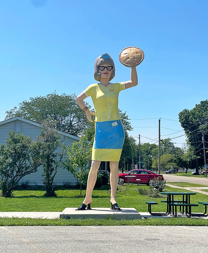 Lumi the Pie Lady holds her pastry aloft like an Olympic torch, her beehive hairdo and cat-eye glasses frozen in mid-century perfection.