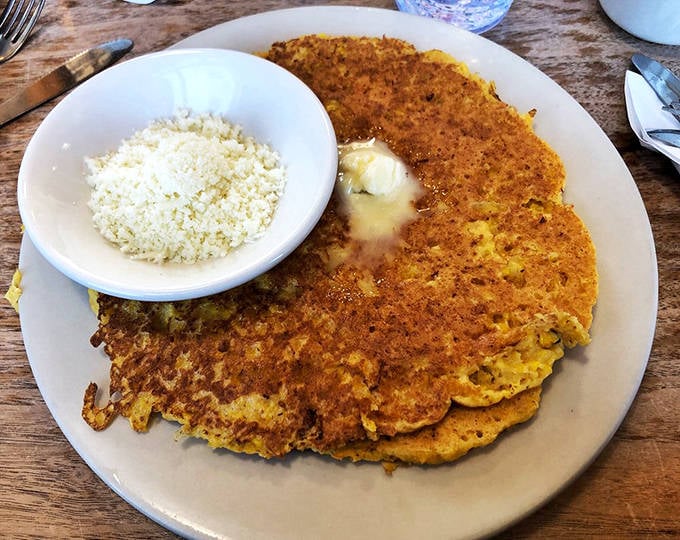 Golden-brown corn pancakes arrive with a side of cotija cheese—a simple presentation that belies the explosion of flavors waiting with each bite.