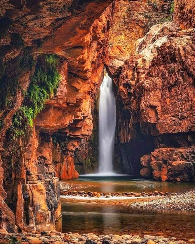 Mother Nature showing off: sunlight illuminates the falls, transforming ordinary water into a luminous curtain against the rust-colored canyon backdrop.