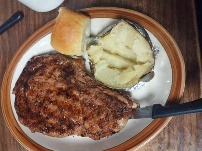 The star of the show: a perfectly cooked ribeye steak alongside a fluffy baked potato and fresh-baked dinner roll.