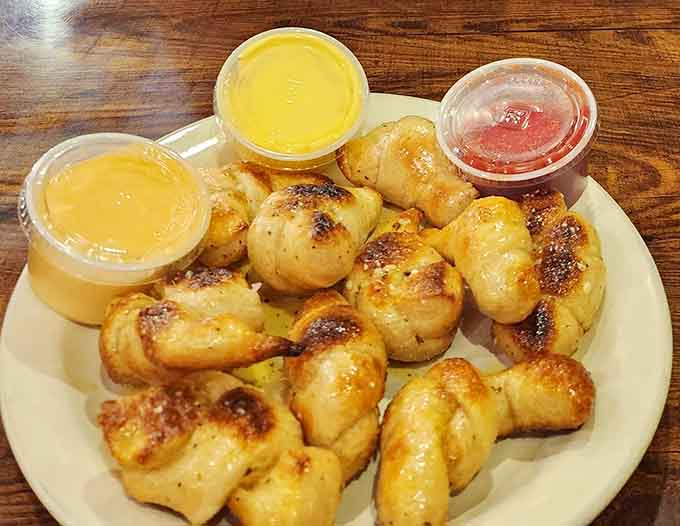 Golden, glistening garlic knots arrive with dipping sauces, ready to ruin your appetite for dinner in the best possible way.