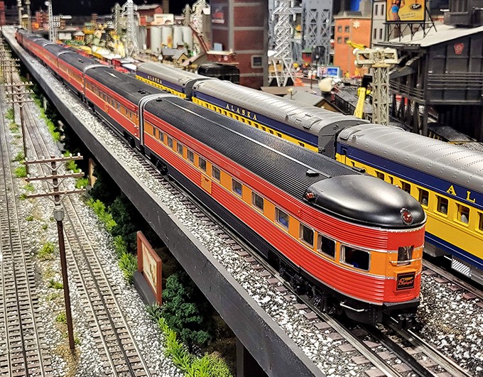 Streamlined passenger cars glide past colorful companions – a rainbow of railroading history in perfect miniature motion.