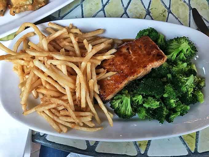 The Citrus BBQ Salmon arrives like a sunset on a plate &ndash; perfectly grilled fish flanked by golden fries and vibrant broccoli for a colorful trio.