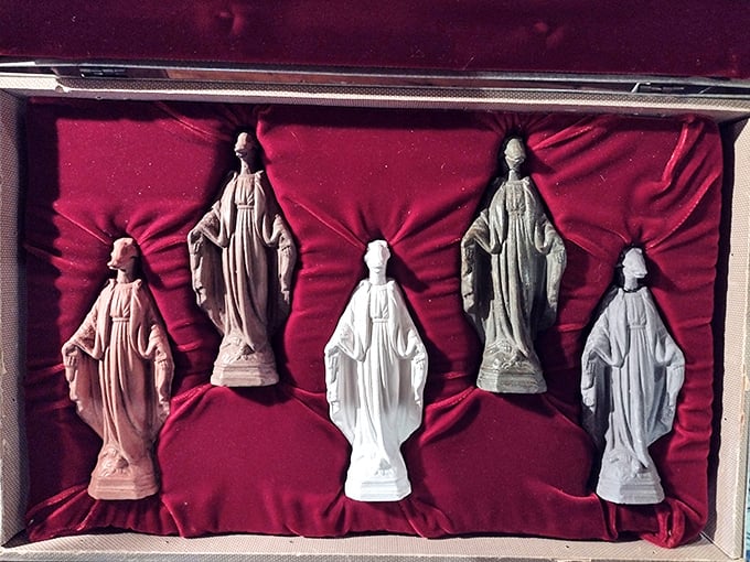 Religious figurines stand at attention against rich red velvet, transforming mass-produced devotional objects into a contemplative art installation.