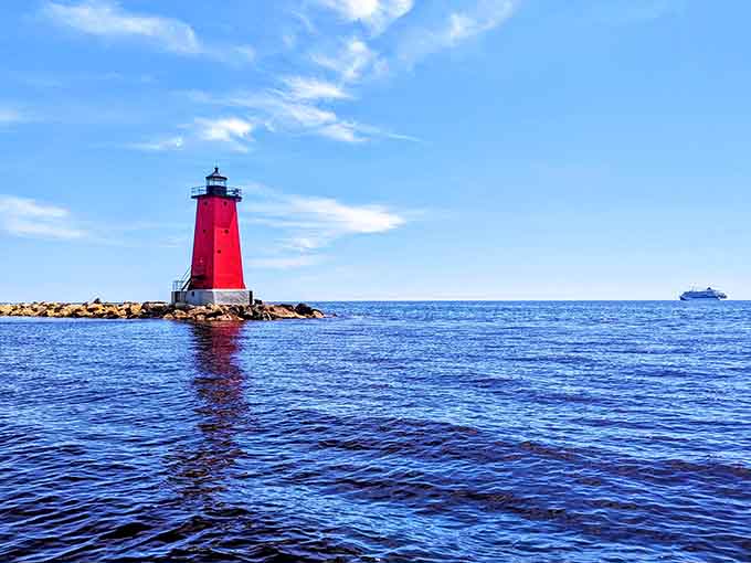 Manistique's crimson lighthouse stands guard where land meets lake, a perfect pop of color against nature's blue canvas.