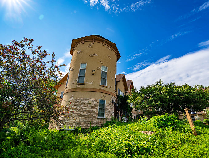 Goldmoor Inn's distinctive round tower rises majestically above the surrounding greenery, its golden-hued stone walls glowing in the sunlight like a beacon for weary royal travelers.