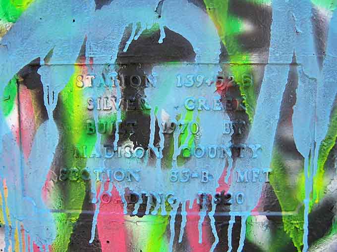 Decades of artistic rebellion preserved on concrete, this plaque barely visible beneath vibrant layers of unauthorized expression.