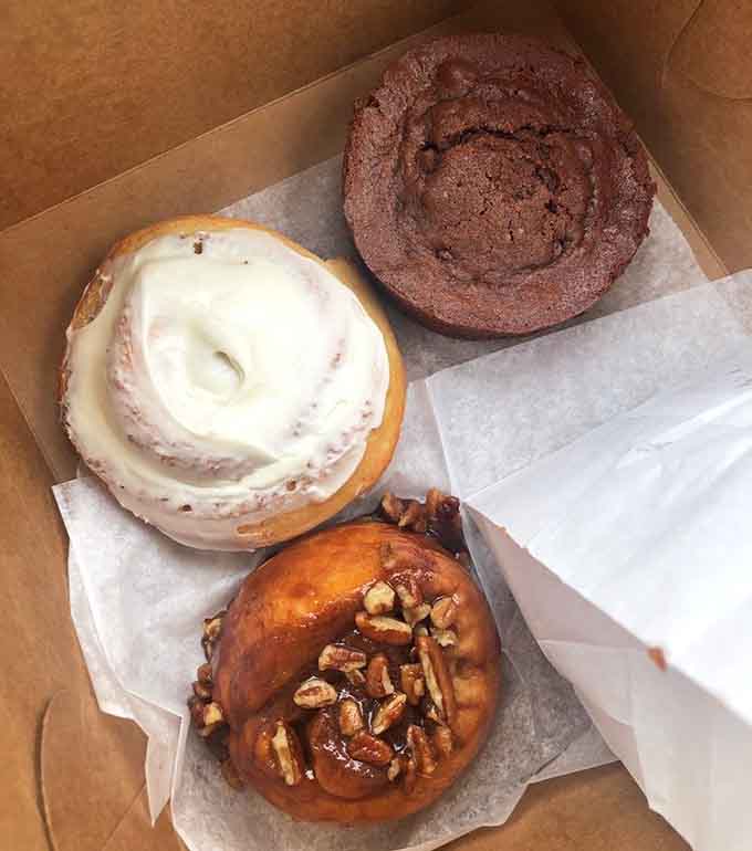 The holy trinity of morning pastries: cinnamon roll, sticky bun, and chocolate coffee cake, each one a masterpiece of butter and sugar.
