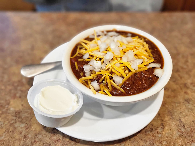 A bowl of homemade chili topped with shredded cheese and diced onions &ndash; winter comfort in a bowl that'll warm you from the inside out.