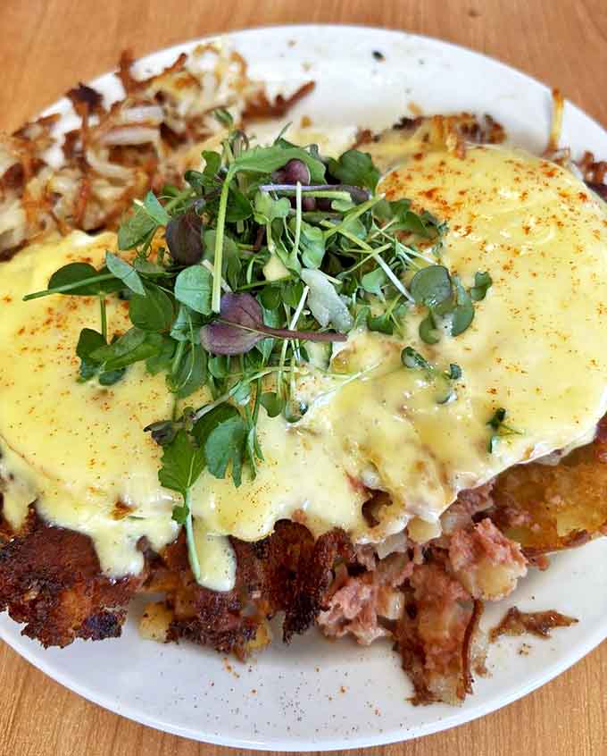 Eggs Timmy transforms the humble English muffin into a throne for perfectly poached eggs and corned beef hash, all crowned with hollandaise royalty.