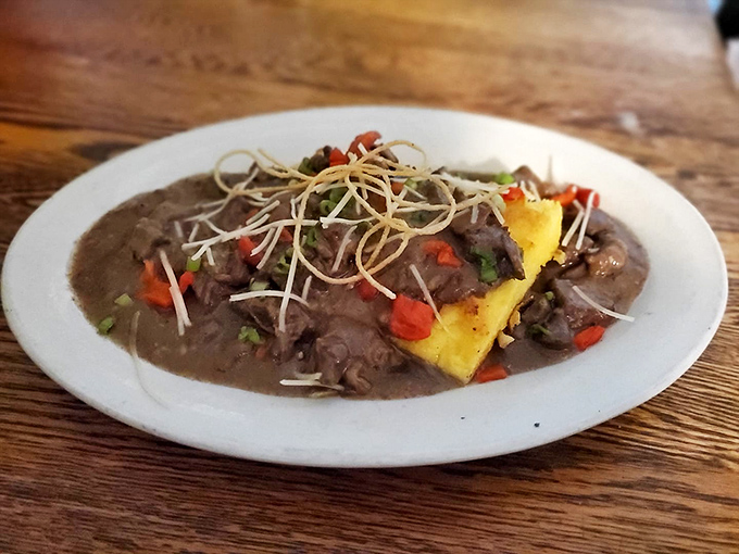 Venison ragout cradles creamy polenta, topped with colorful vegetables and crispy garnish &ndash; a rustic yet refined dish that captures Vermont's wild spirit on a plate.