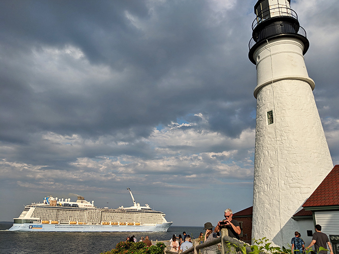 Visitors gather to witness maritime history firsthand, their silhouettes framed against dramatic skies and the iconic white tower.