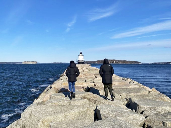Adventurous visitors navigate the granite breakwater, their journey to the lighthouse becoming part of the experience rather than just the destination.