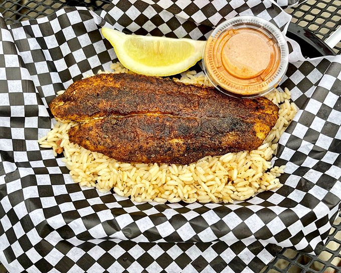 Blackened catfish resting on a bed of rice &ndash; the crisp, spice-crusted exterior giving way to flaky, tender fish beneath.