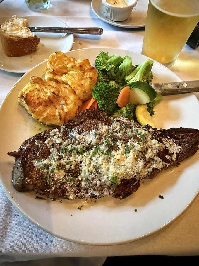 The ribeye wears its char marks like medals of honor, topped with a blue cheese crust that melts into the meat's natural juices. Vegetable companions add color and contrast.