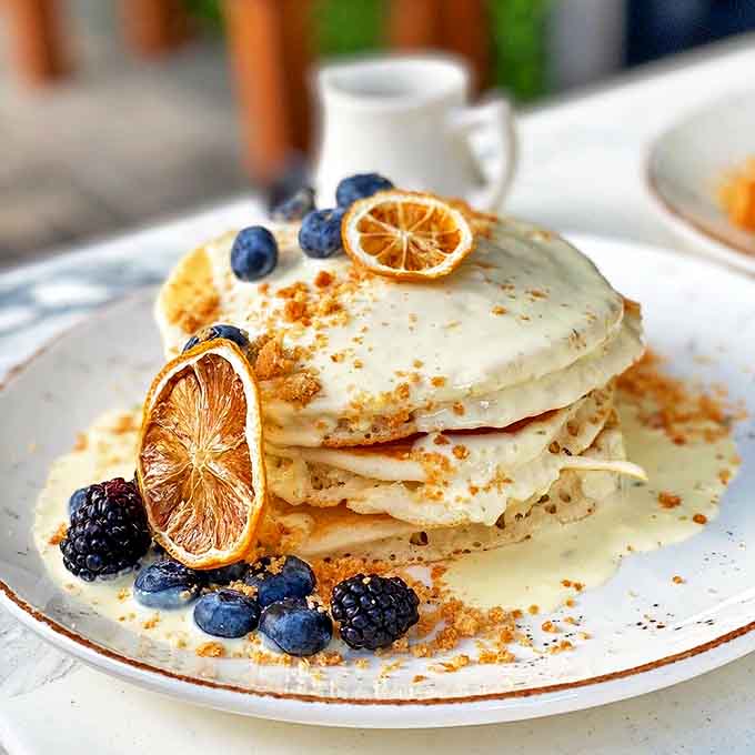 Key lime pancakes that capture Florida sunshine on a plate &ndash; fluffy discs crowned with berries, citrus, and what appears to be graham cracker dust.