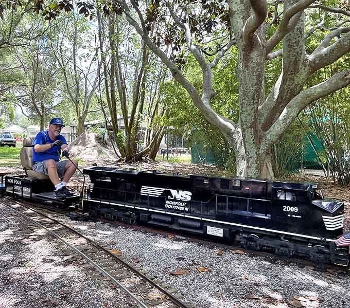 The engineer carefully navigates the controls, his blue uniform and cap completing the authentic railroad experience that delights visitors monthly.