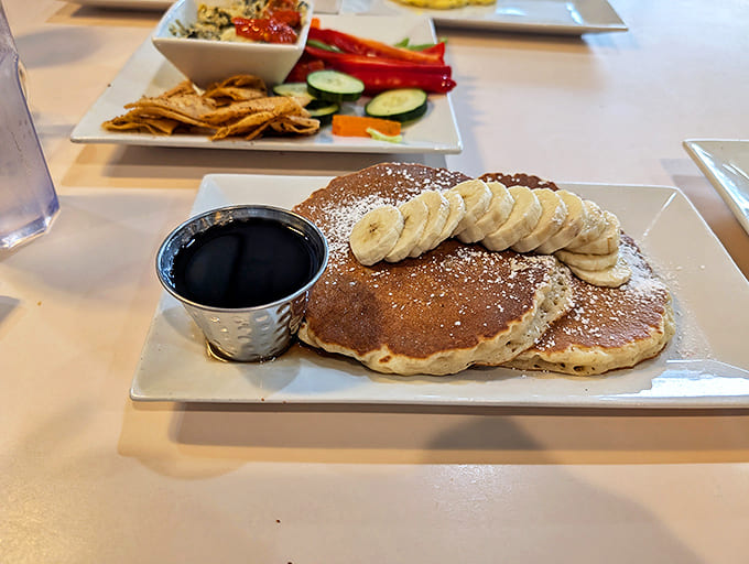 Fluffy pancakes topped with fresh banana slices and a generous dusting of powdered sugar, served with syrup for those sweet morning cravings.