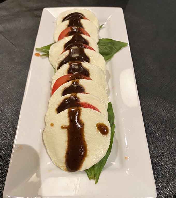 Fresh mozzarella meets ripe tomatoes in this caprese presentation, drizzled with balsamic like an edible work of art on a plate.