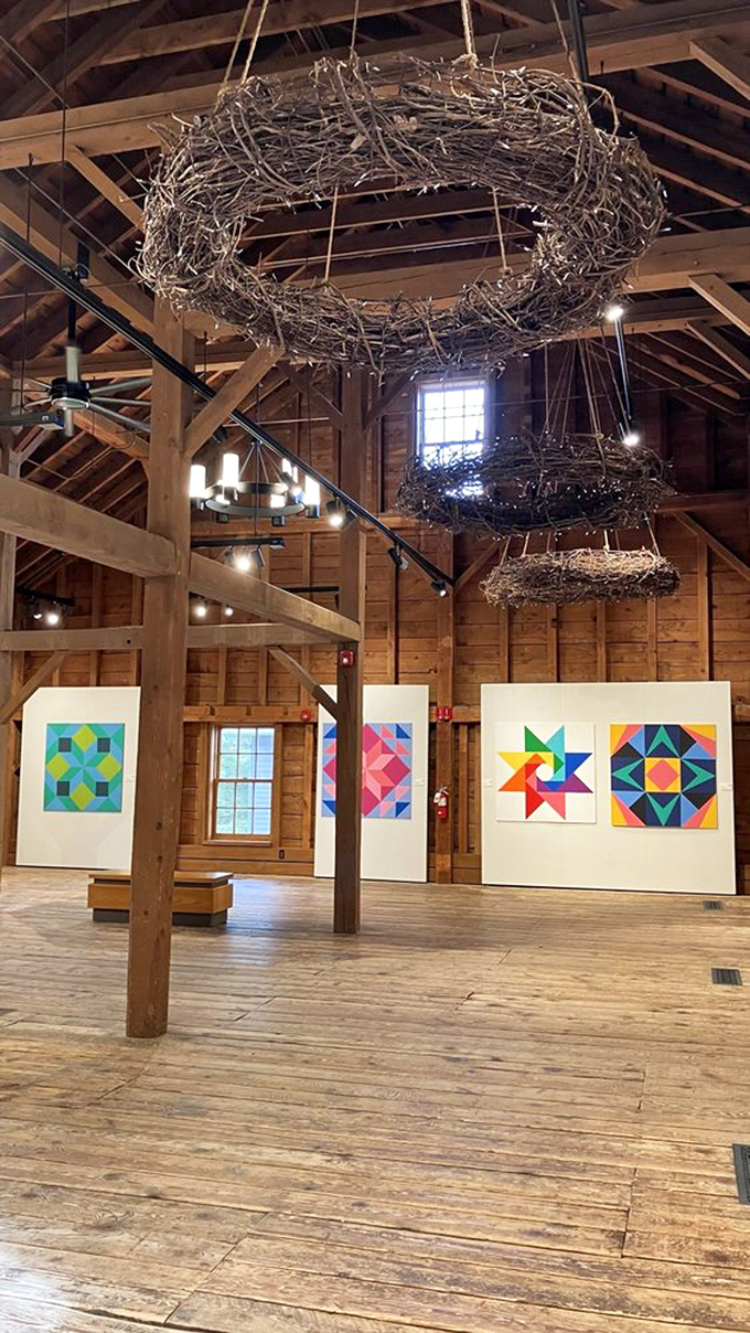 Art meets agriculture under rustic rafters, where handcrafted nest-like chandeliers hover above vibrant quilt displays that tell stories through fabric instead of words.