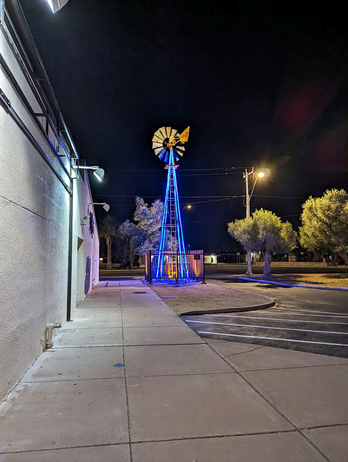 The blue-illuminated windmill stands tall against the night sky, spinning tales of desert prosperity and agricultural dreams from Arizona's not-so-distant past.