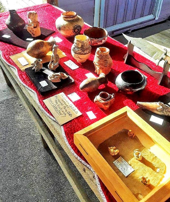 Ancient pottery pieces rest on vibrant red cloth, their earthy tones and primitive designs connecting modern shoppers to artisans from centuries past.
