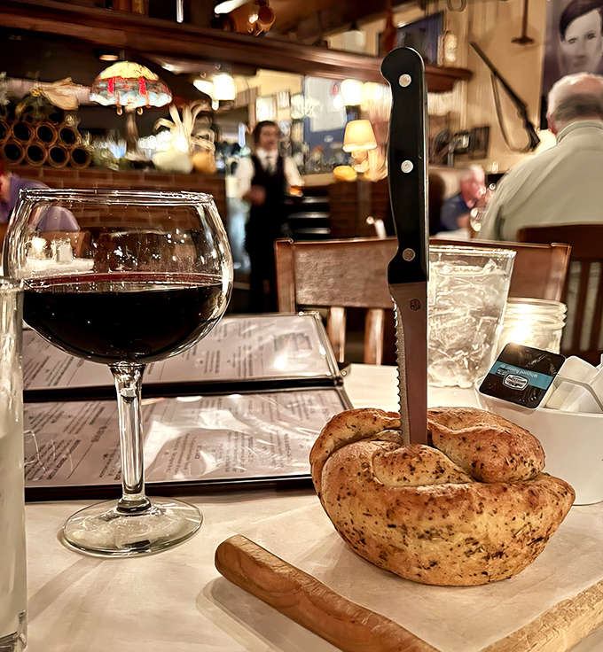 A glass of robust red wine stands guard beside fresh-baked bread – the perfect opening act before the main event, like a culinary warm-up band that could headline elsewhere.