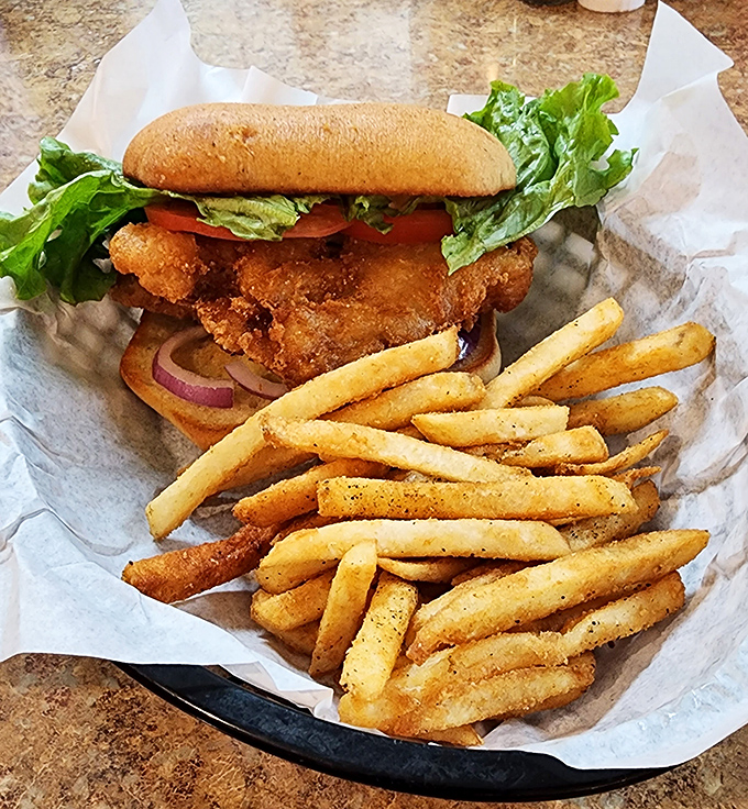 A golden, crispy chicken sandwich piled high with fresh lettuce and tomatoes&mdash;served with a generous helping of seasoned fries for the perfect diner comfort meal.