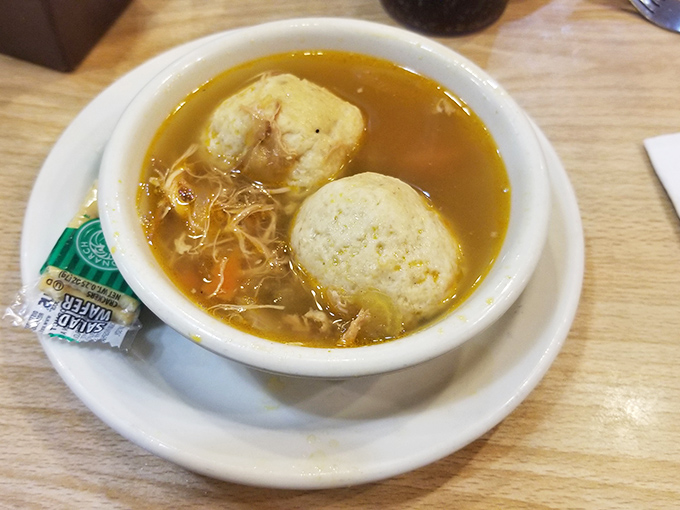 Liquid gold chicken broth cradles tender vegetables and matzo balls that achieve the perfect balance – substantial without being heavy, seasoned with generations of know-how.