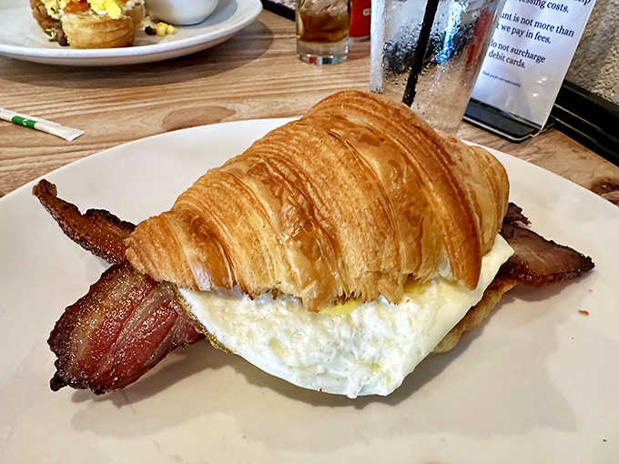 This isn't just any breakfast sandwich &ndash; it's architectural breakfast brilliance with applewood bacon peeking out from a golden croissant.