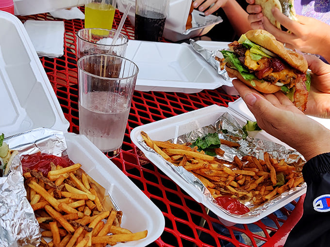 Golden fries nestled beside a perfectly assembled burger &ndash; the outdoor red tables provide the ideal setting for this classic American meal under blue skies.