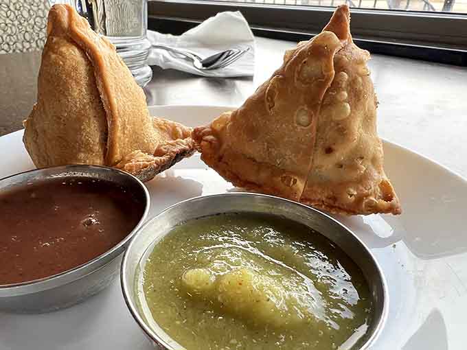 Crispy samosas filled with spiced potatoes arrive with vibrant chutneys, proving that the perfect appetizer exists and it's shaped like a triangle.