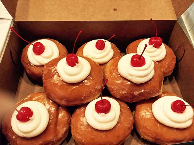 Glazed donuts topped with cream and cherries, looking like they escaped from a 1950s diner in the best way.