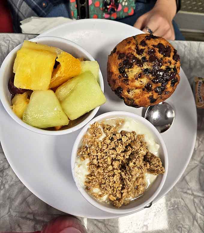A holy trinity of morning delights: fresh fruit, blueberry muffin, and yogurt &ndash; virtue and indulgence on one plate.