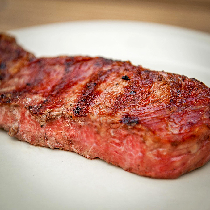 The New York Strip arrives like a meaty masterpiece &ndash; perfectly cross-hatched grill marks promising the kind of flavor that makes conversation stop mid-sentence.