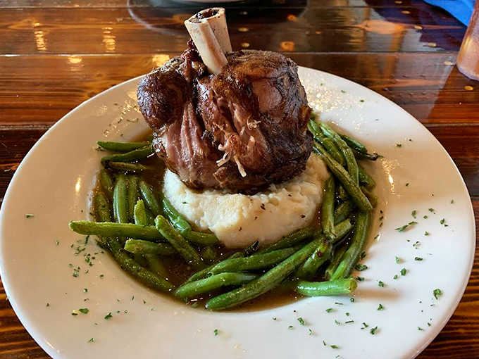 Fall-off-the-bone tender pork perches atop creamy mashed potatoes, surrounded by vibrant green beans and a rich, savory sauce.