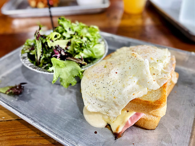 The Croque sandwich sits regally beside fresh greens, a sophisticated comfort food ambassador that bridges diner classics and French bistro elegance.