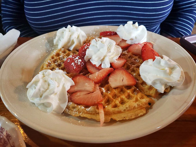 Fresh strawberries nestled on a waffle with clouds of whipped cream &ndash; nature's candy meets breakfast perfection.