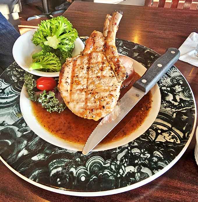 This bone-in pork chop arrives perfectly grilled, accompanied by fresh vegetables that prove side dishes deserve respect too.