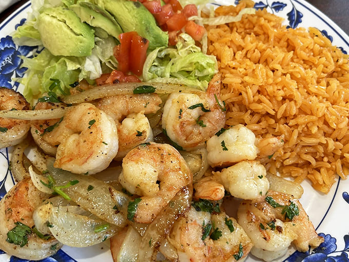 Perfectly cooked shrimp dance with onions and herbs, accompanied by the restaurant's signature rice and a fresh salad – simple perfection on a plate.