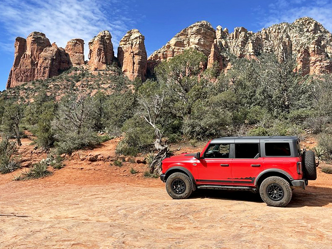 A bright red vehicle provides perfect scale against the towering red rock formations, like a toy car in nature's magnificent playground.